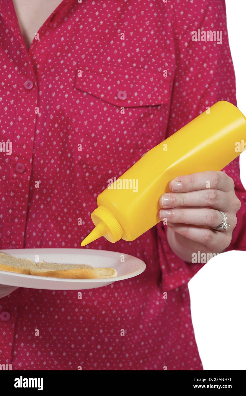 Woman squeezing a mustard condiment on a bun Stock Photo - Alamy