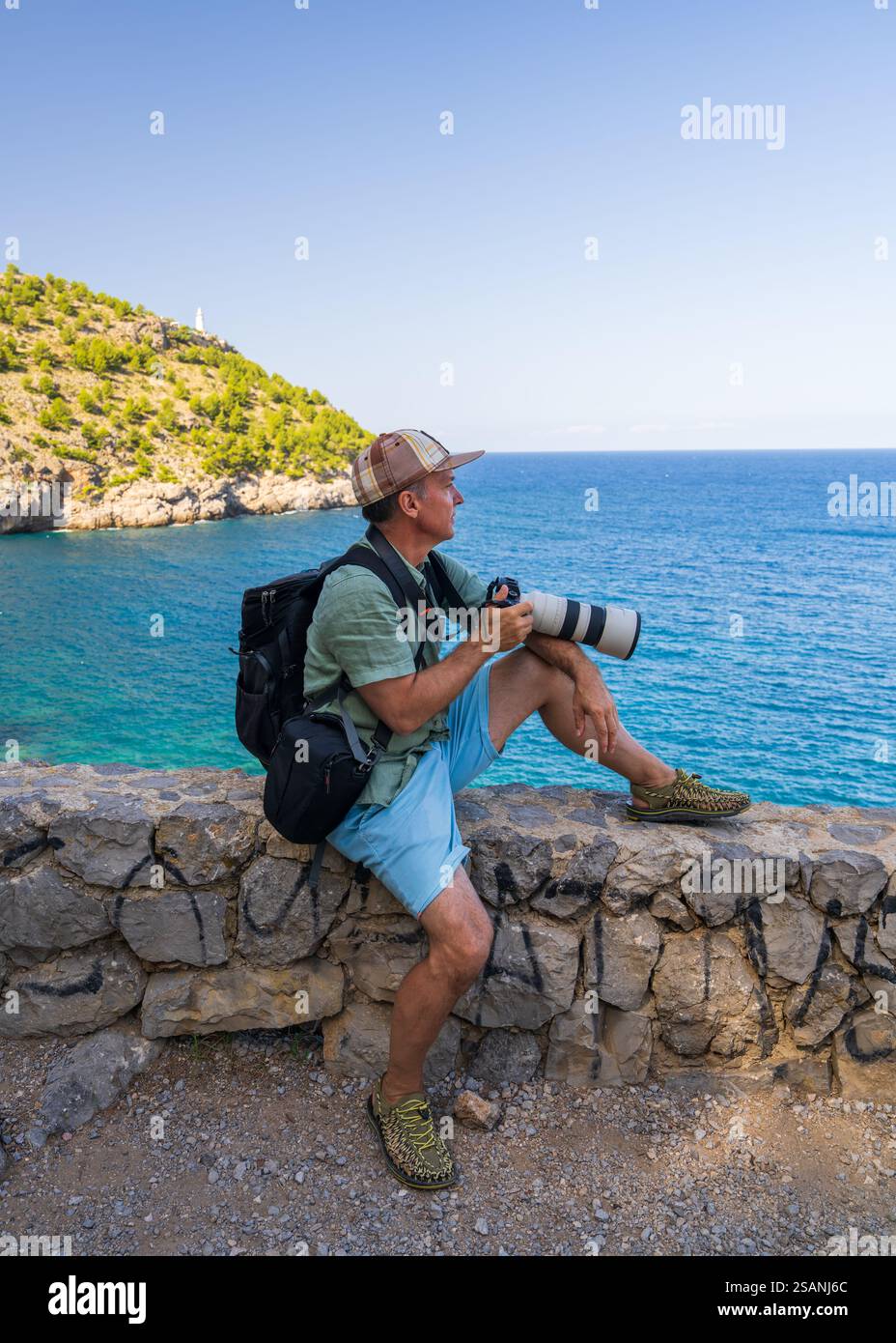 Travel photographer with professional camera sits on stone fence and ...