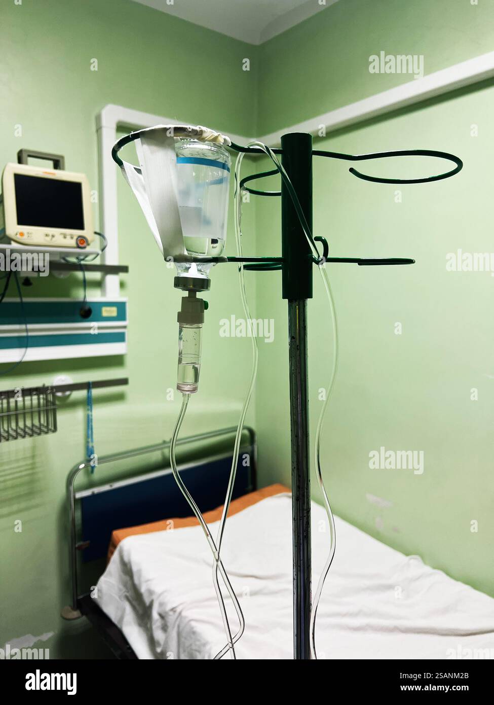 A hospital room featuring a single bed, IV drip equipment, and a ...
