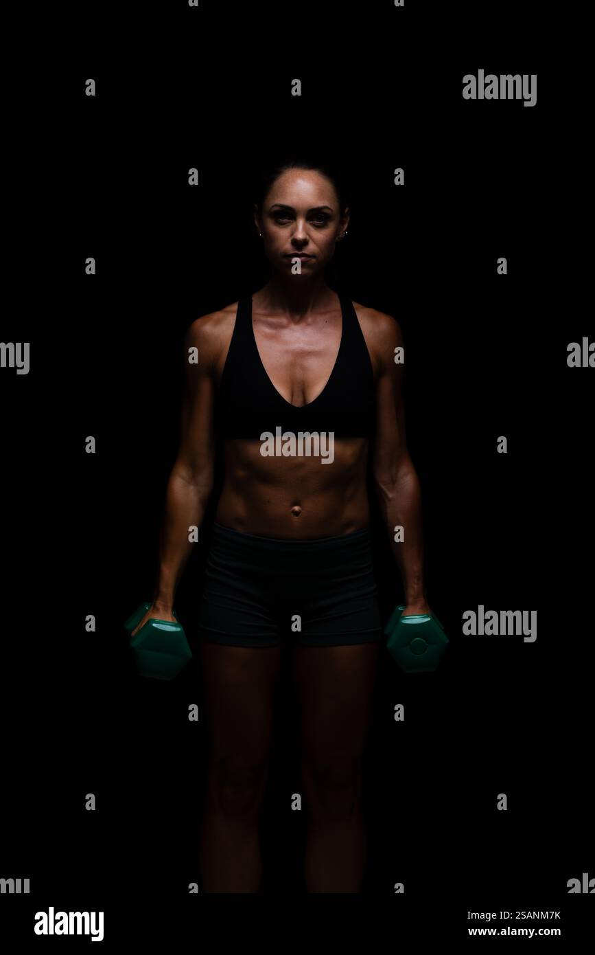 Athlete in a black workout outfit exercises with green dumbbells in a ...