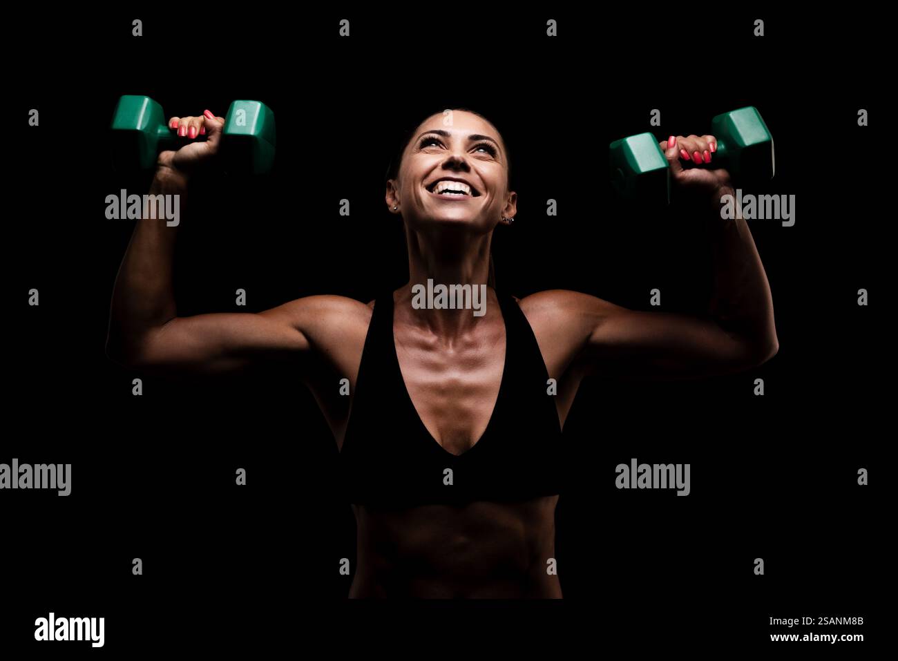 A strong and confident woman exercises by lifting green dumbbells ...