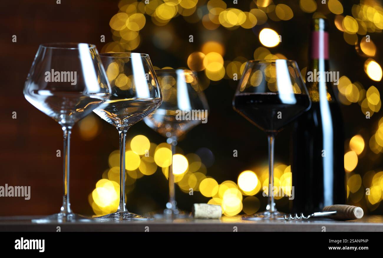 Glass with red wine and empty ones on table against blurred lights ...