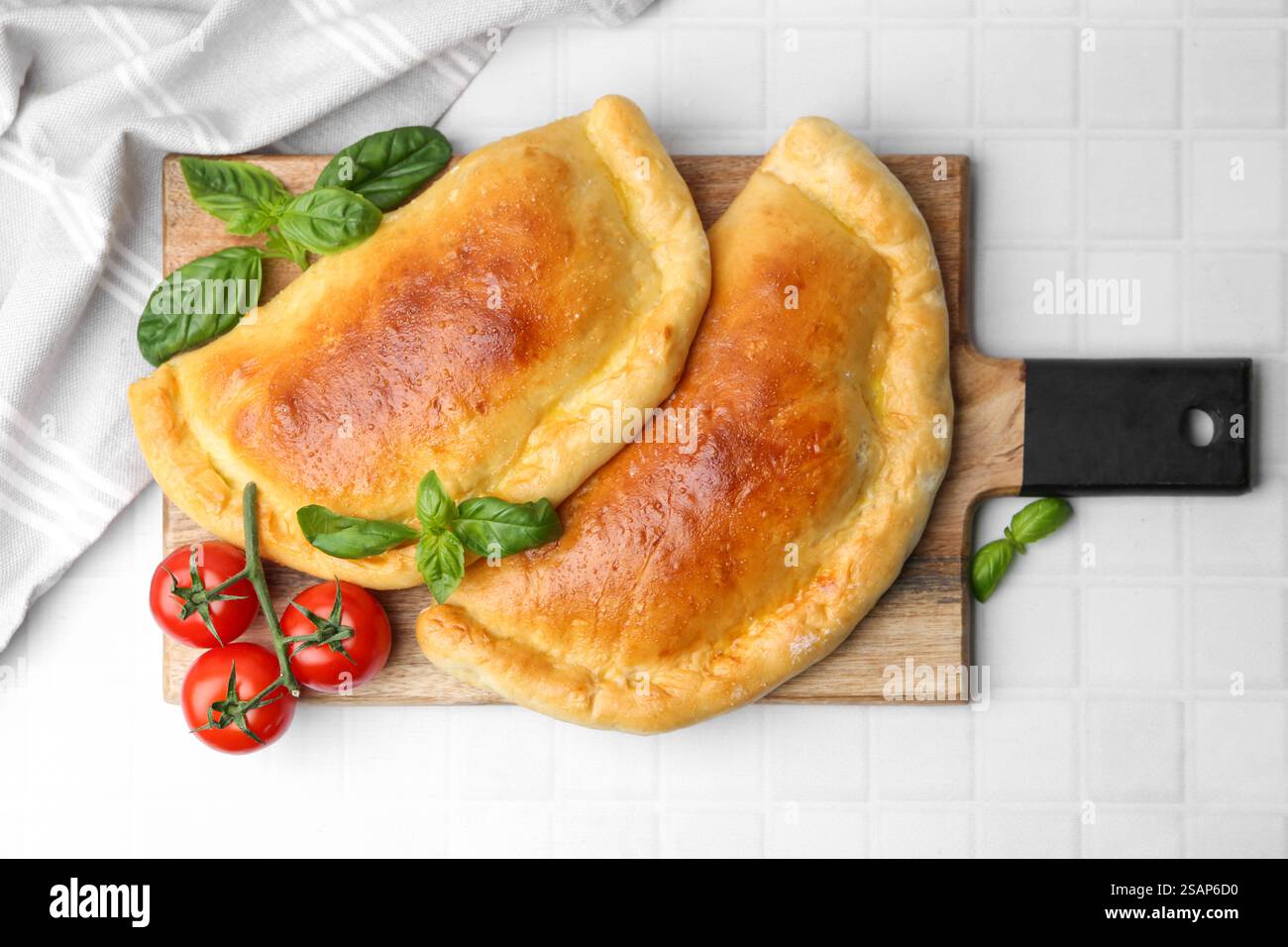 Tasty vegetarian calzones with basil and tomatoes on white tiled table ...