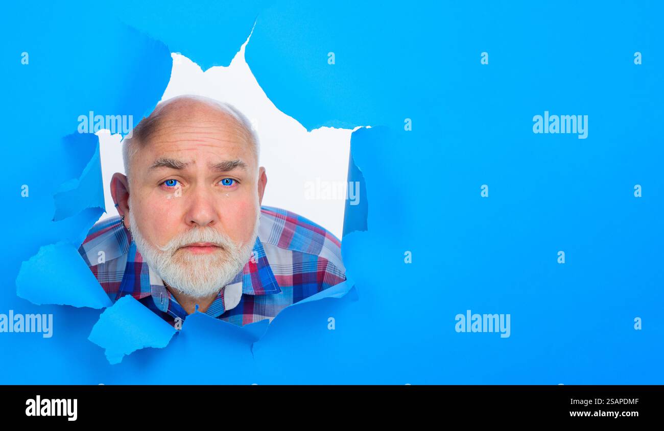 Bearded man with blue color lenses in eyes looking through hole in ...