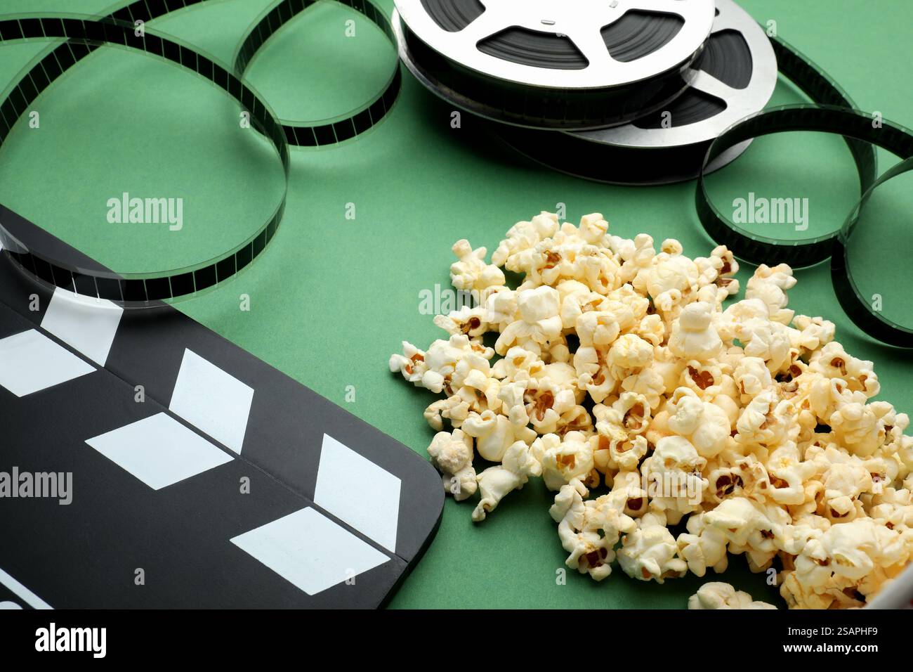 Movie clapper, tasty popcorn and film reel on green background, closeup ...