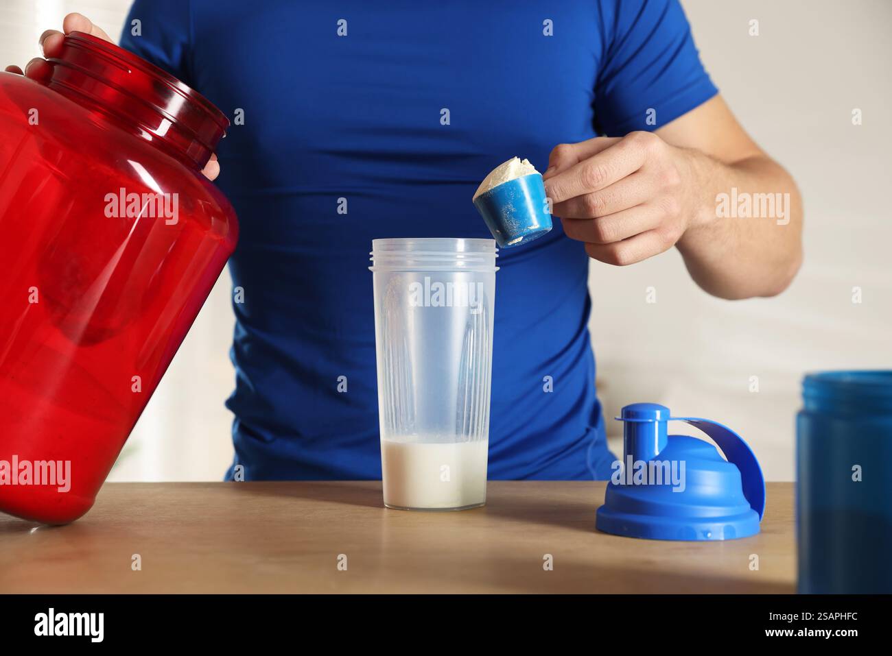 Making protein cocktail. Man adding powder into shaker at wooden table ...