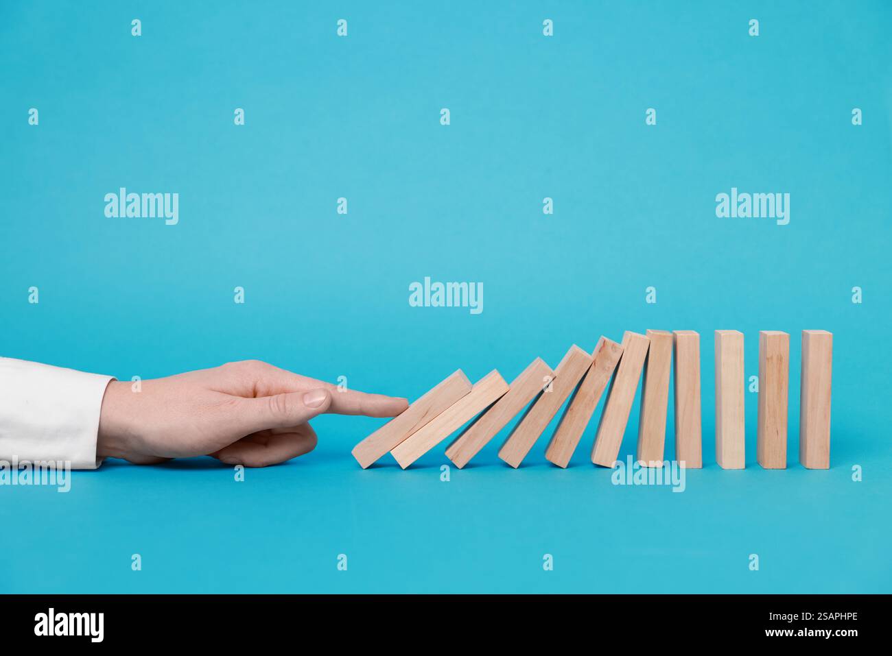 Domino effect. Woman pushing wooden blocks on light blue background ...