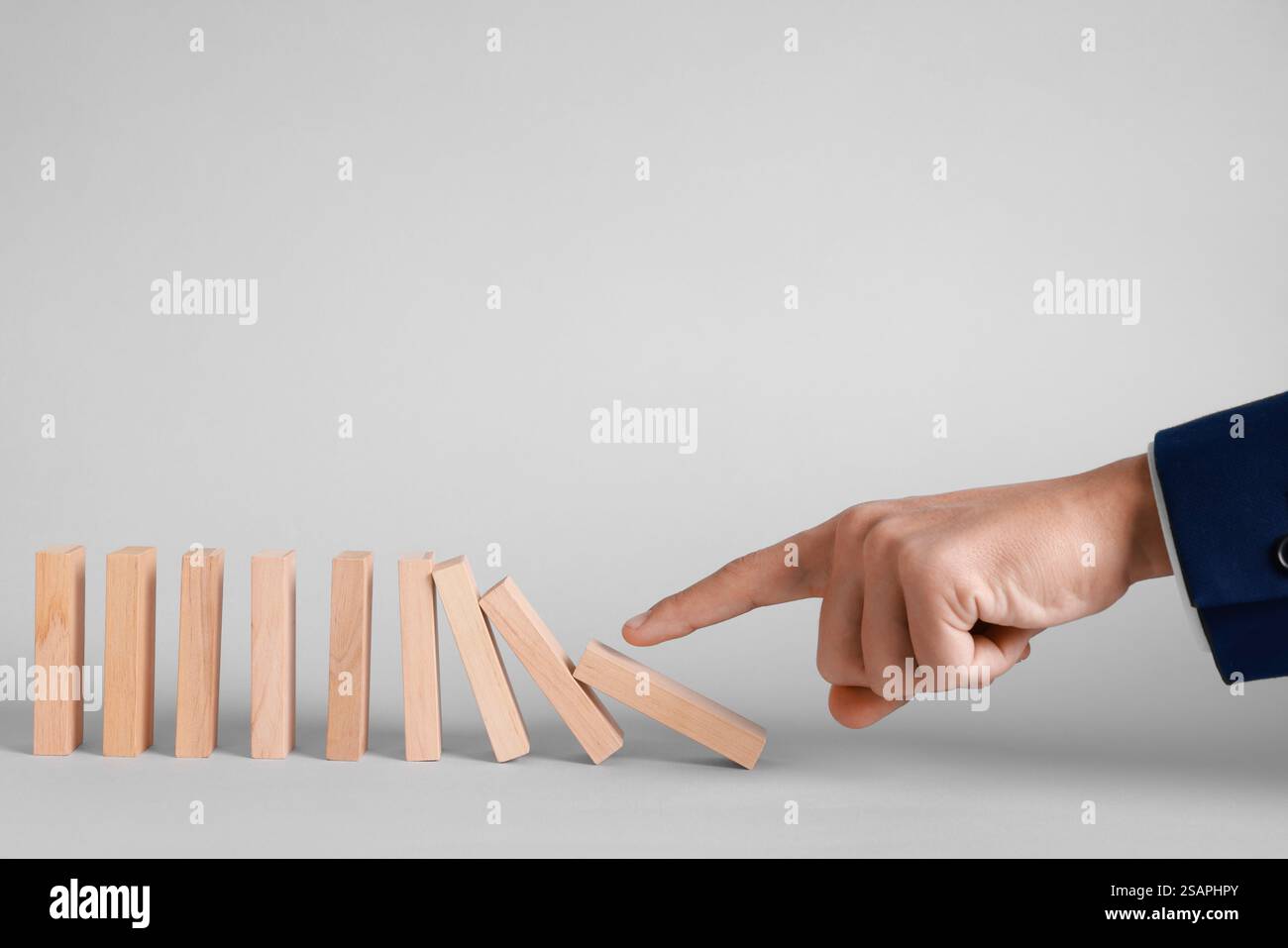Domino effect. Man pushing wooden blocks on light background, closeup ...