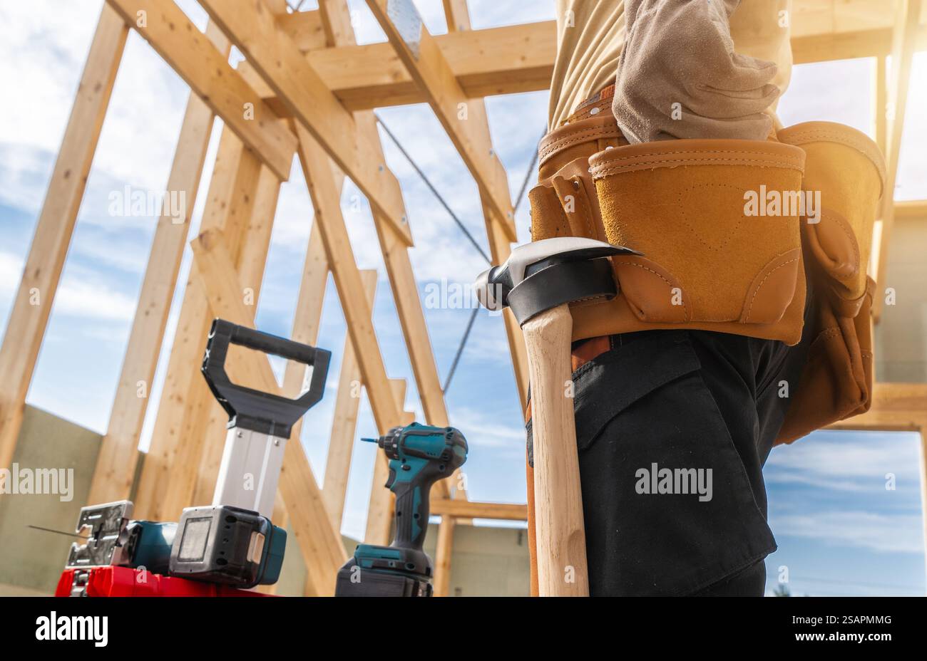 A construction worker stands at a building site, wearing a tool belt ...