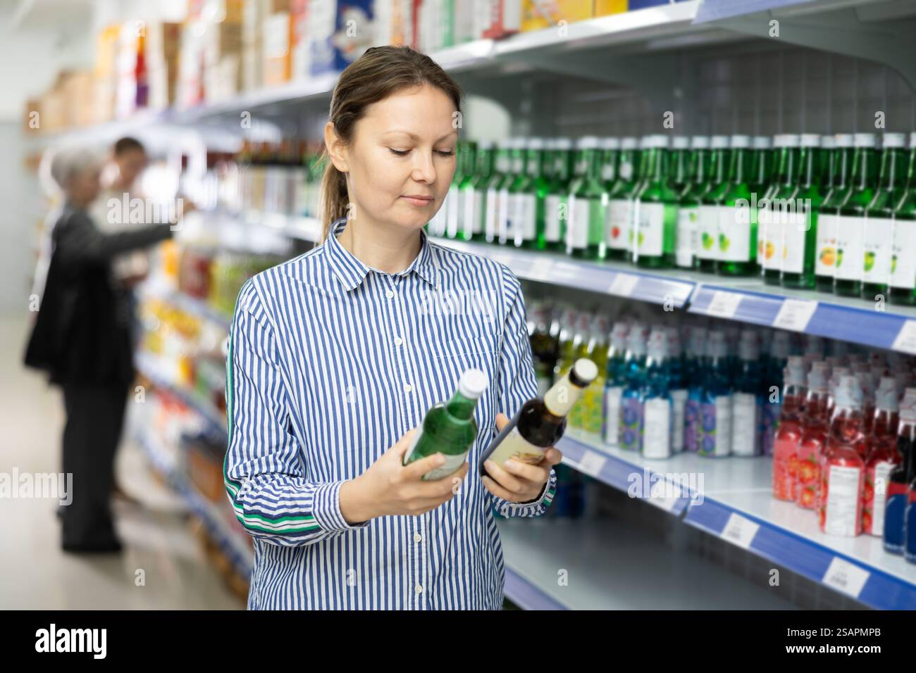 Positive woman reading label on bottle of Korean soju in Asian store ...