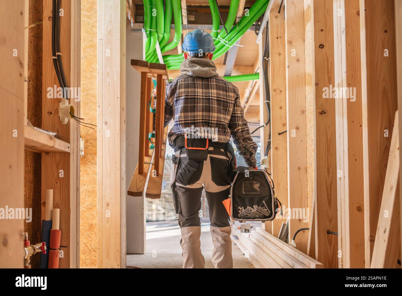 A construction worker carries tools while walking through a wooden ...