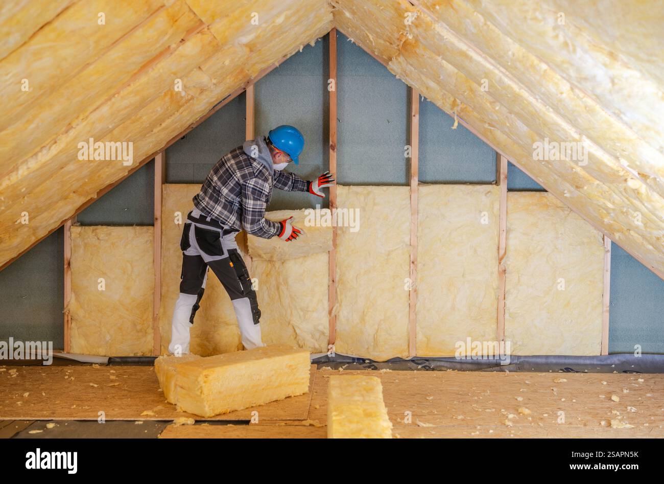 A worker wearing a helmet and gloves is installing mineral wool ...