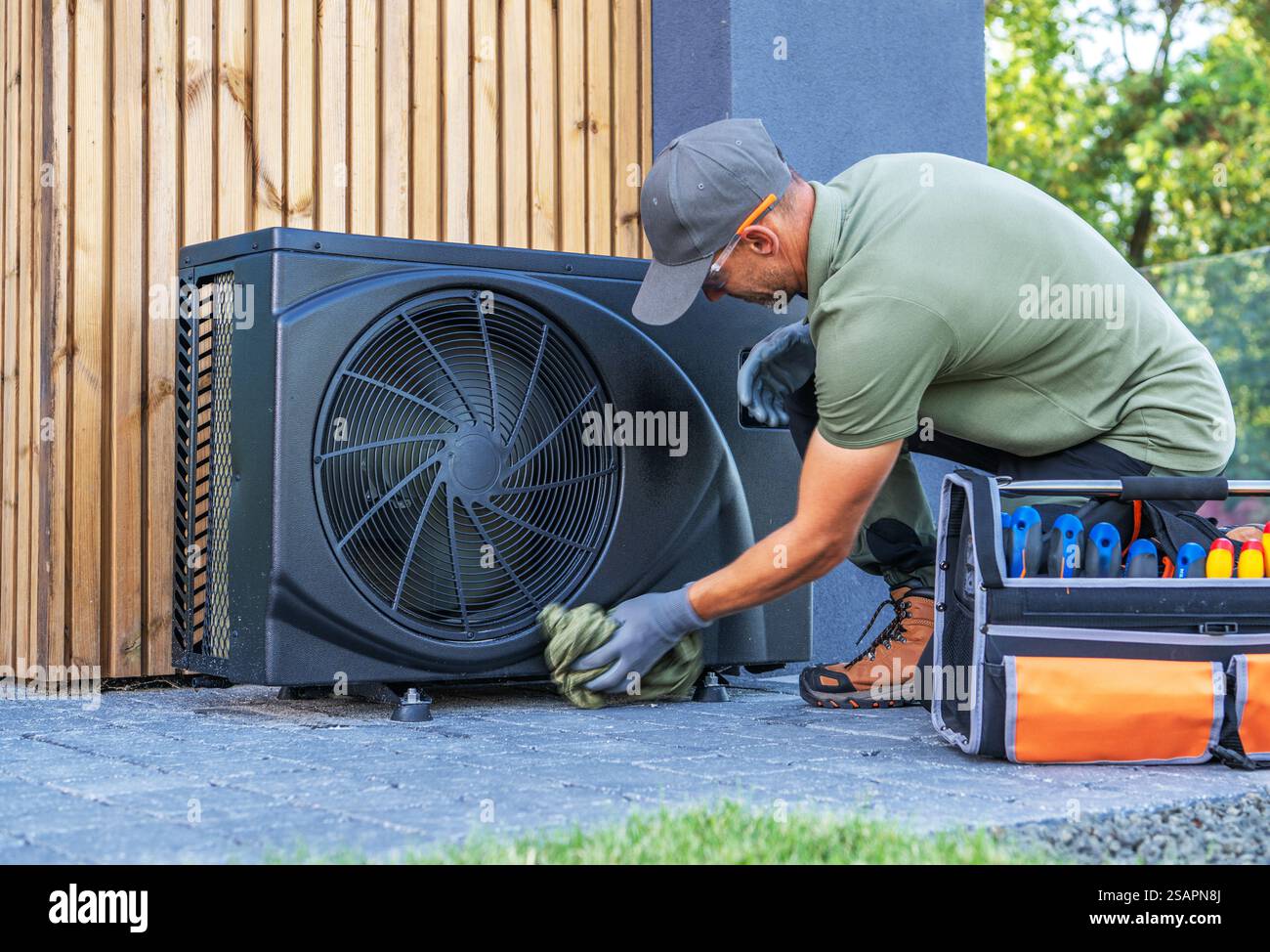 A technician in work attire cleans an outdoor air conditioning unit ...