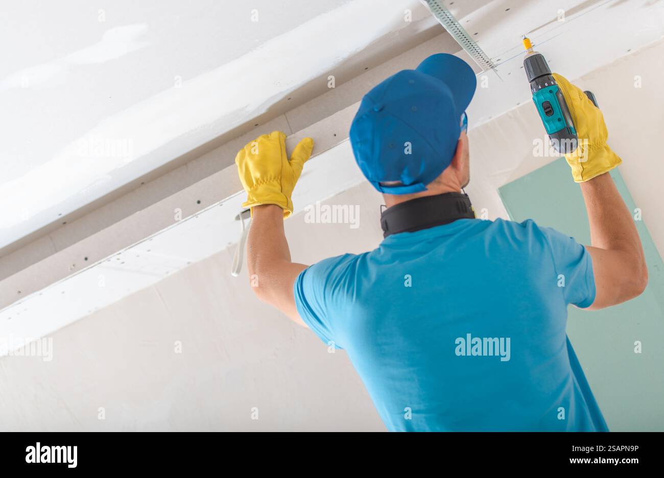 A diligent worker wearing gloves and a cap uses a drill to install ...