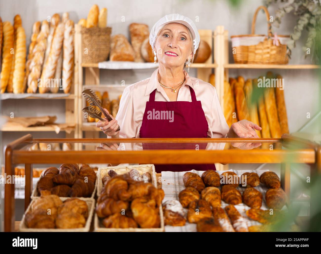senior bakery worker sells croissants and shows off a variety of ...