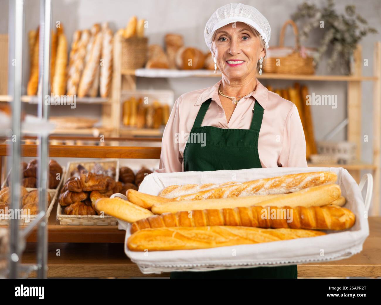 Smiling mature female seller showing assortment of bakery Stock Photo ...