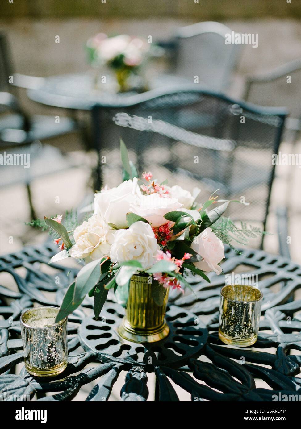 A charming arrangement of white roses and greenery sits in a golden ...