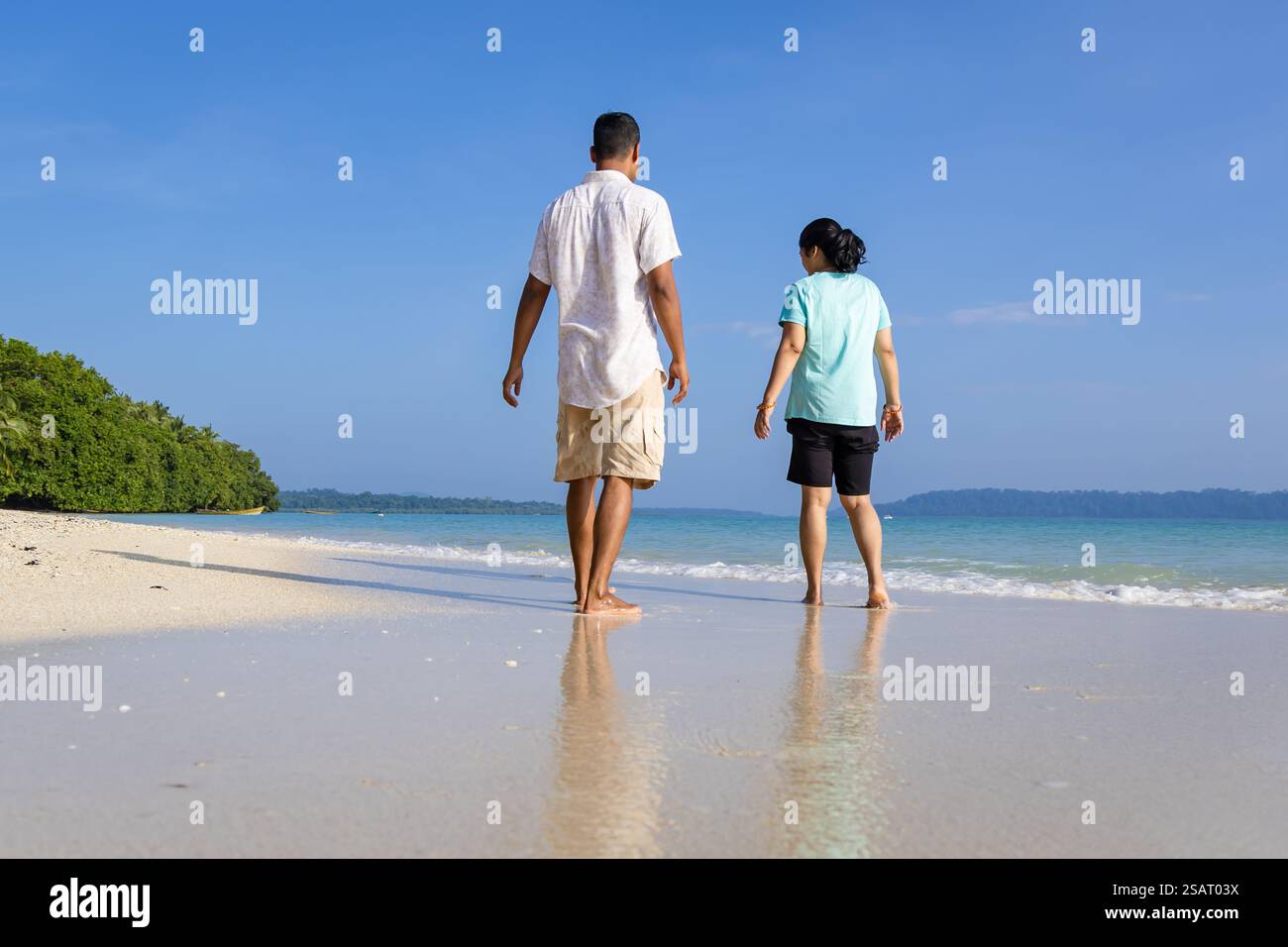 married couple romantic walk strolling along beach with rolling waves at morning image is taken ...
