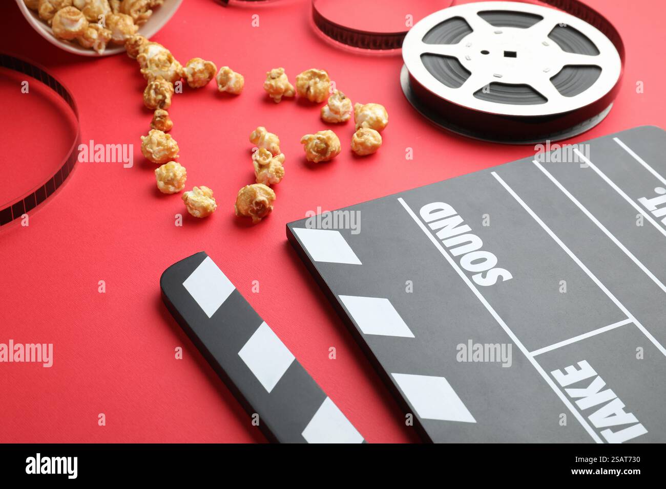 Movie clapper, sweet popcorn and film reel on red background, closeup ...