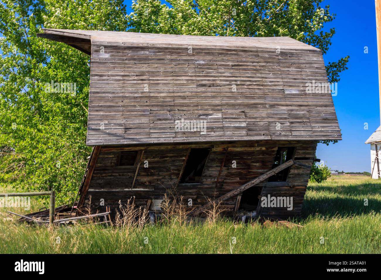 A large, old barn with a slanted roof sits in a grassy field. The barn ...