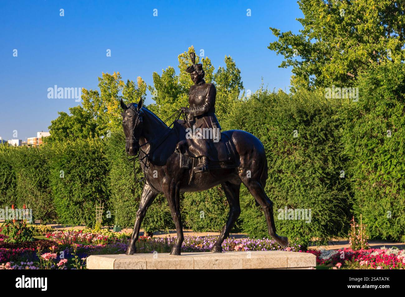 A statue of a woman riding a horse in a park. The statue is black and ...