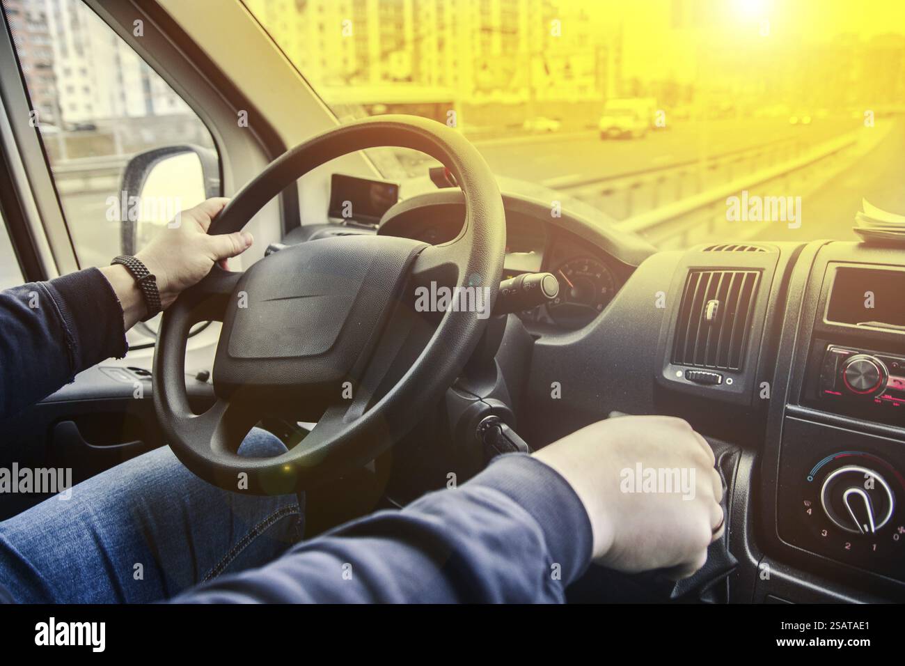 Driver operating a vehicle during sunset, cityscape visible through ...