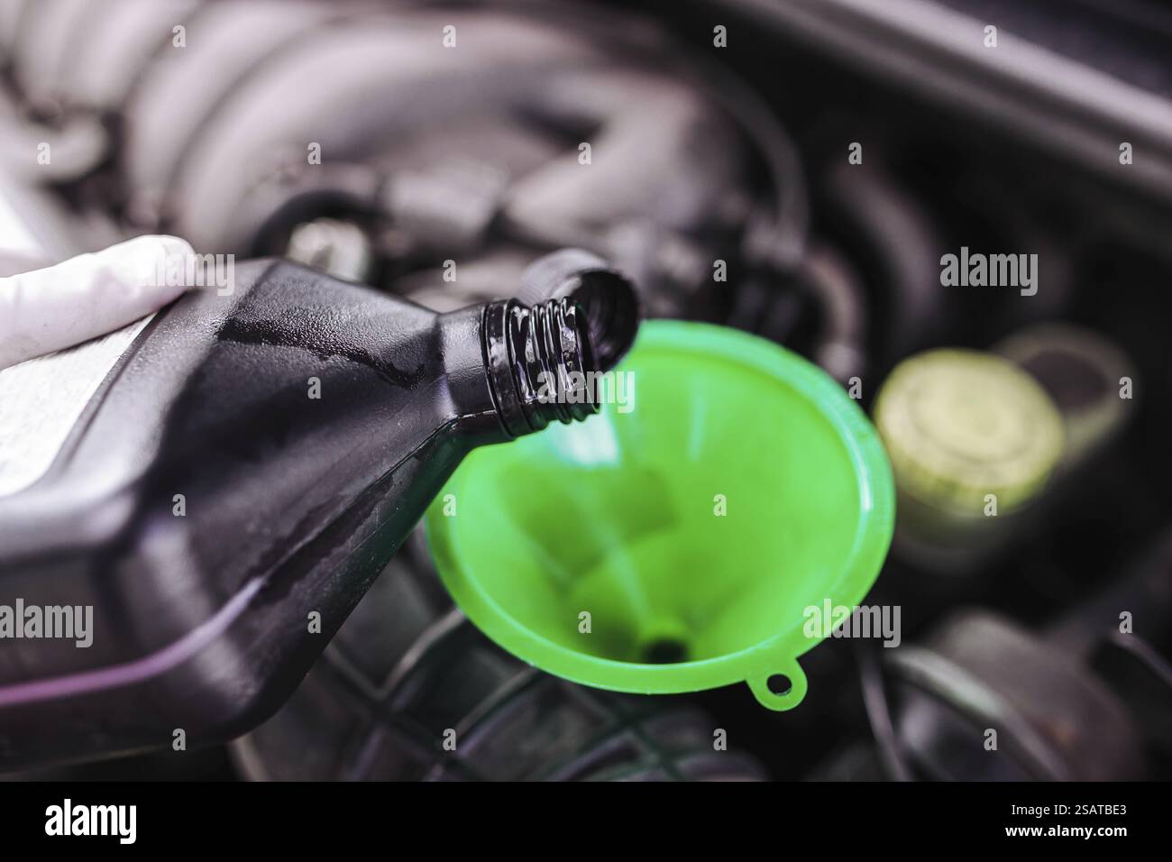 Pouring fluid into a car engine using a green funnel and black bottle ...