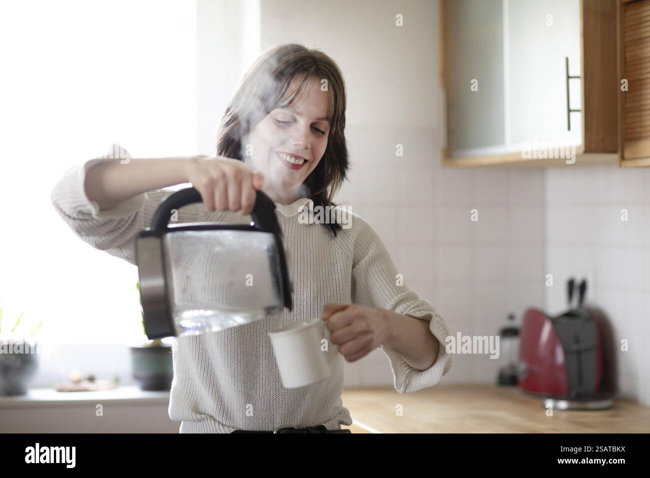 Woman smiles while pouring water into a cup with a kettle, saving ...