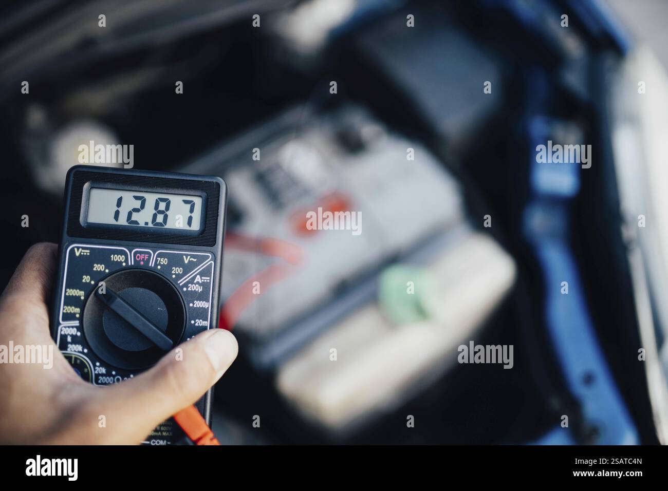 Hand holding a voltmeter measuring car battery voltage, digits ...