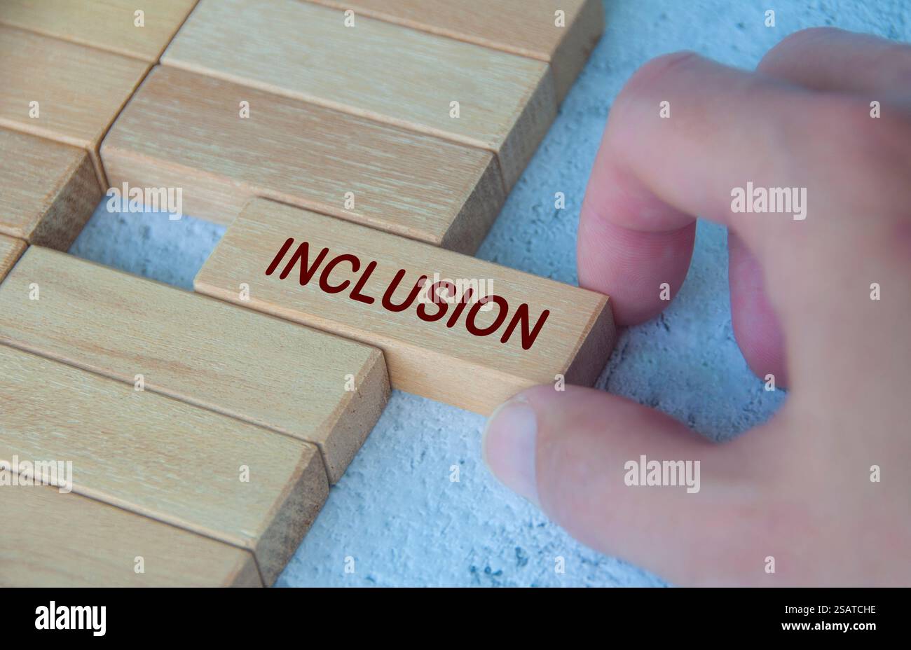 Hand placing Inclusion text on wooden blocks surrounded by other wooden ...