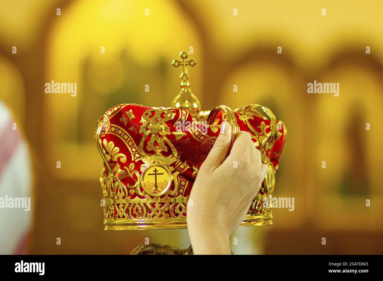Hand holding a richly decorated red and gold crown inside a church ...