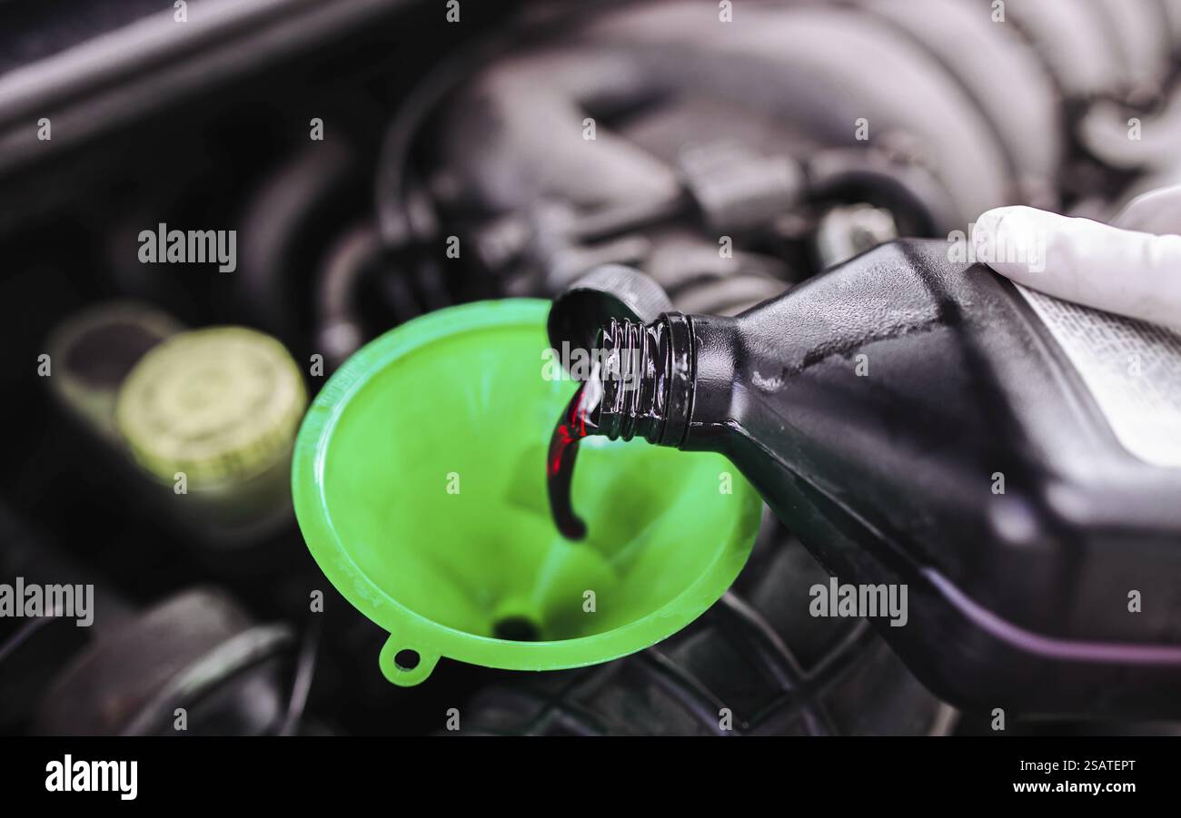 Oil being carefully poured into a car's engine using a green funnel ...