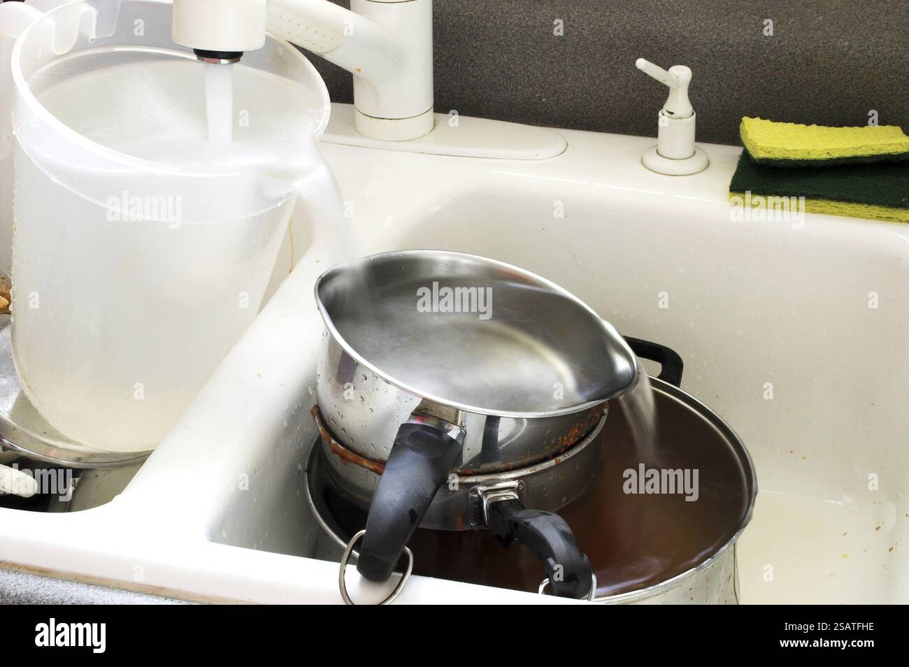 Water from a spigot creating a waterfall in a sink of pots and pans ...