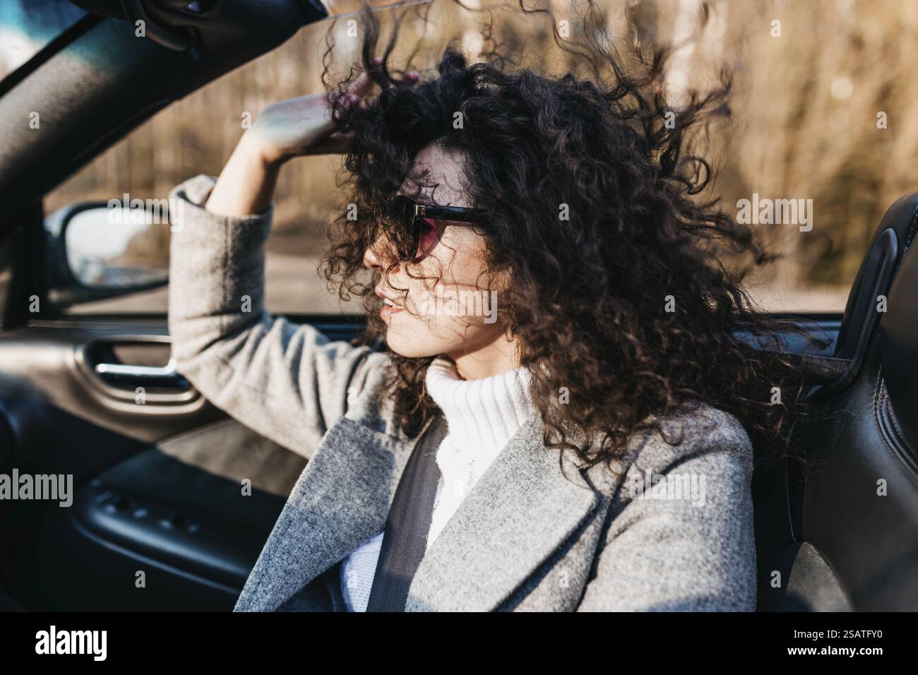 Dynamic scene of a woman enjoying the wind in a convertible, expressing ...