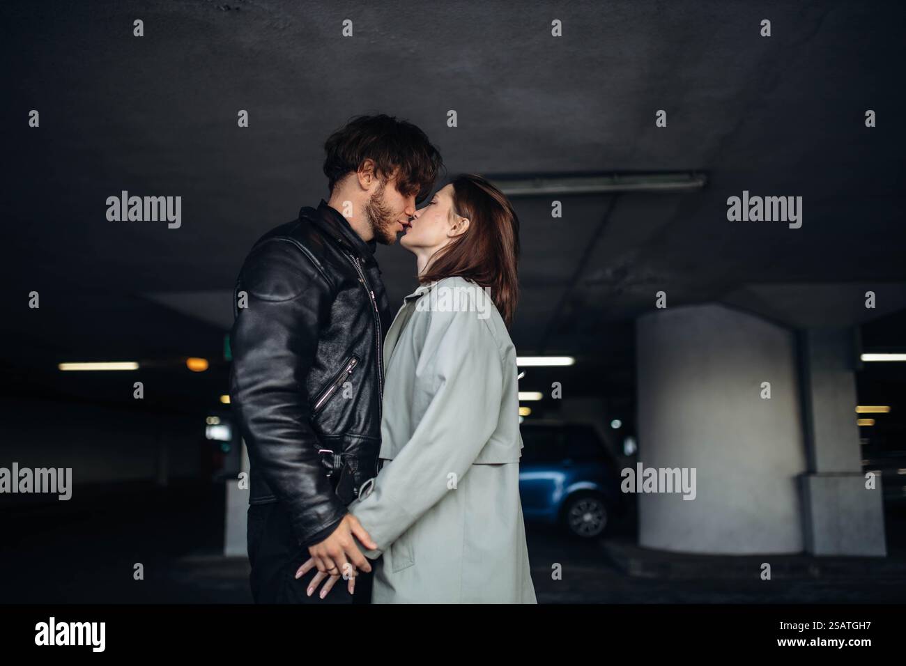 The couple shares a kiss in a dimly lit parking garage, showing ...