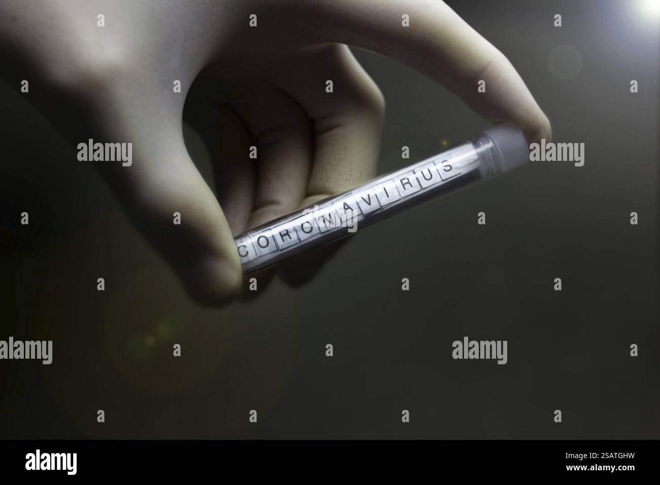 Hand in a glove holding a coronavirus-labeled test tube in dim light ...
