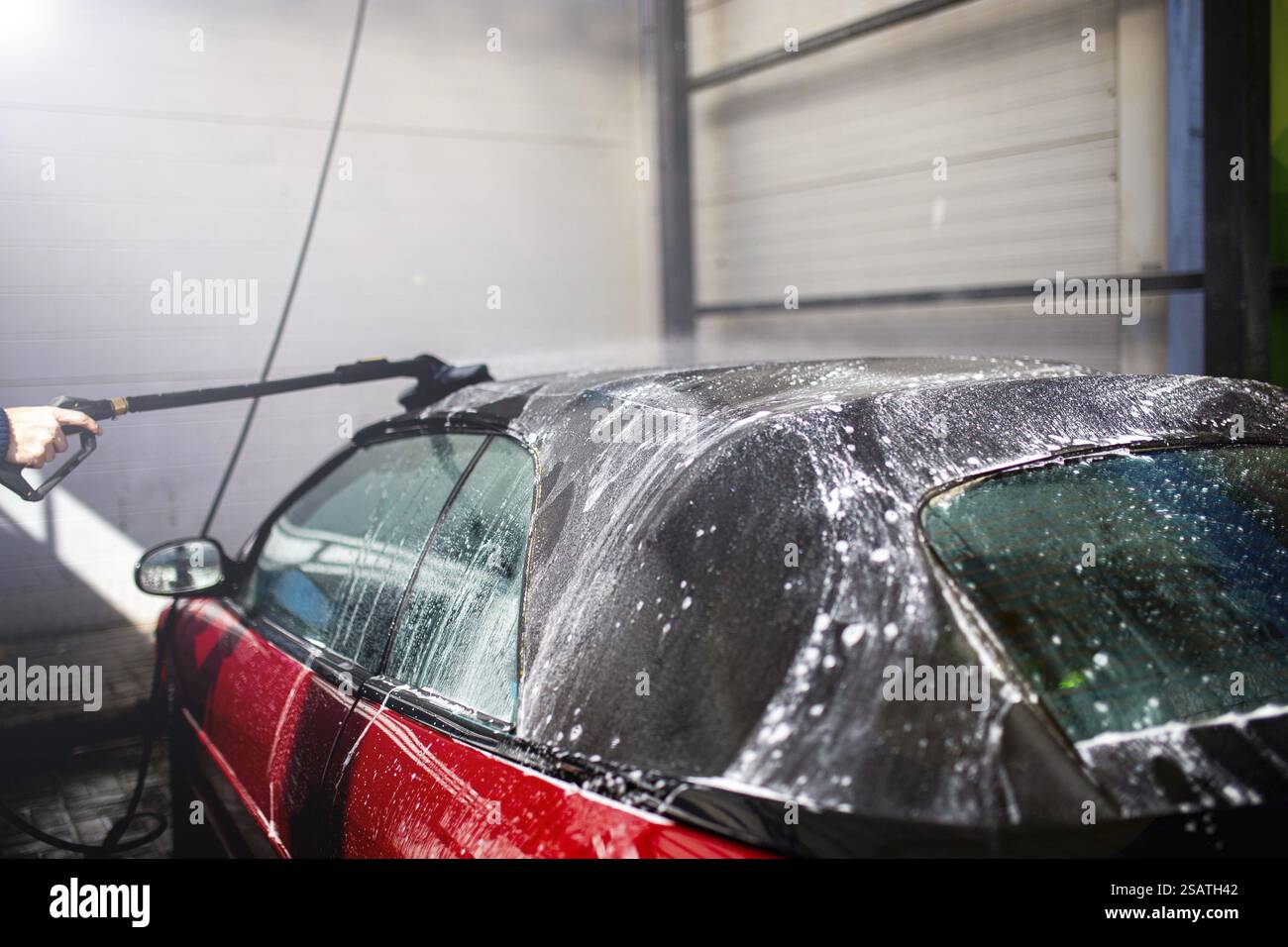 Rinsing soap off the roof of a red car using a pressure washer inside a ...