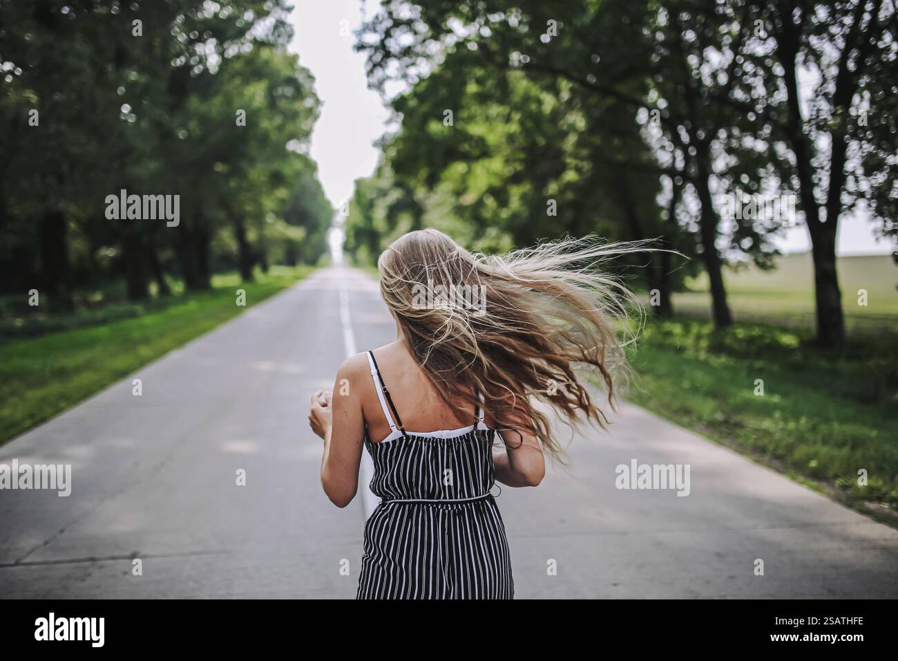 Back view of a woman walking dynamically on a forest road with hair in ...