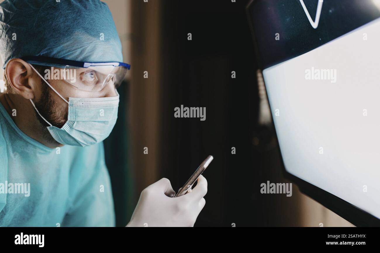 Surgeon glancing at phone beside an illuminated x-ray Stock Photo - Alamy