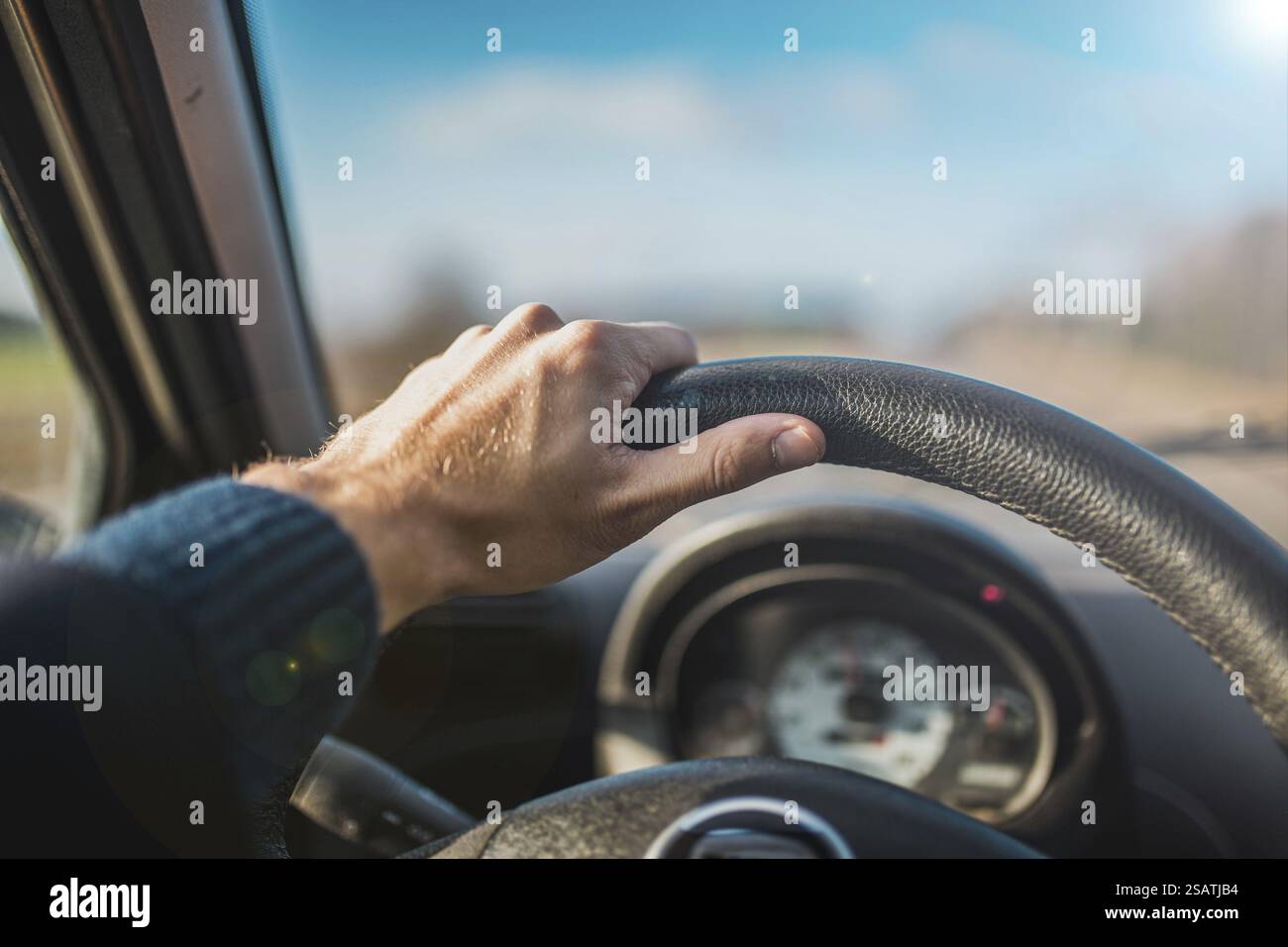 Hand on a steering wheel with a clear blue sky visible through the car ...