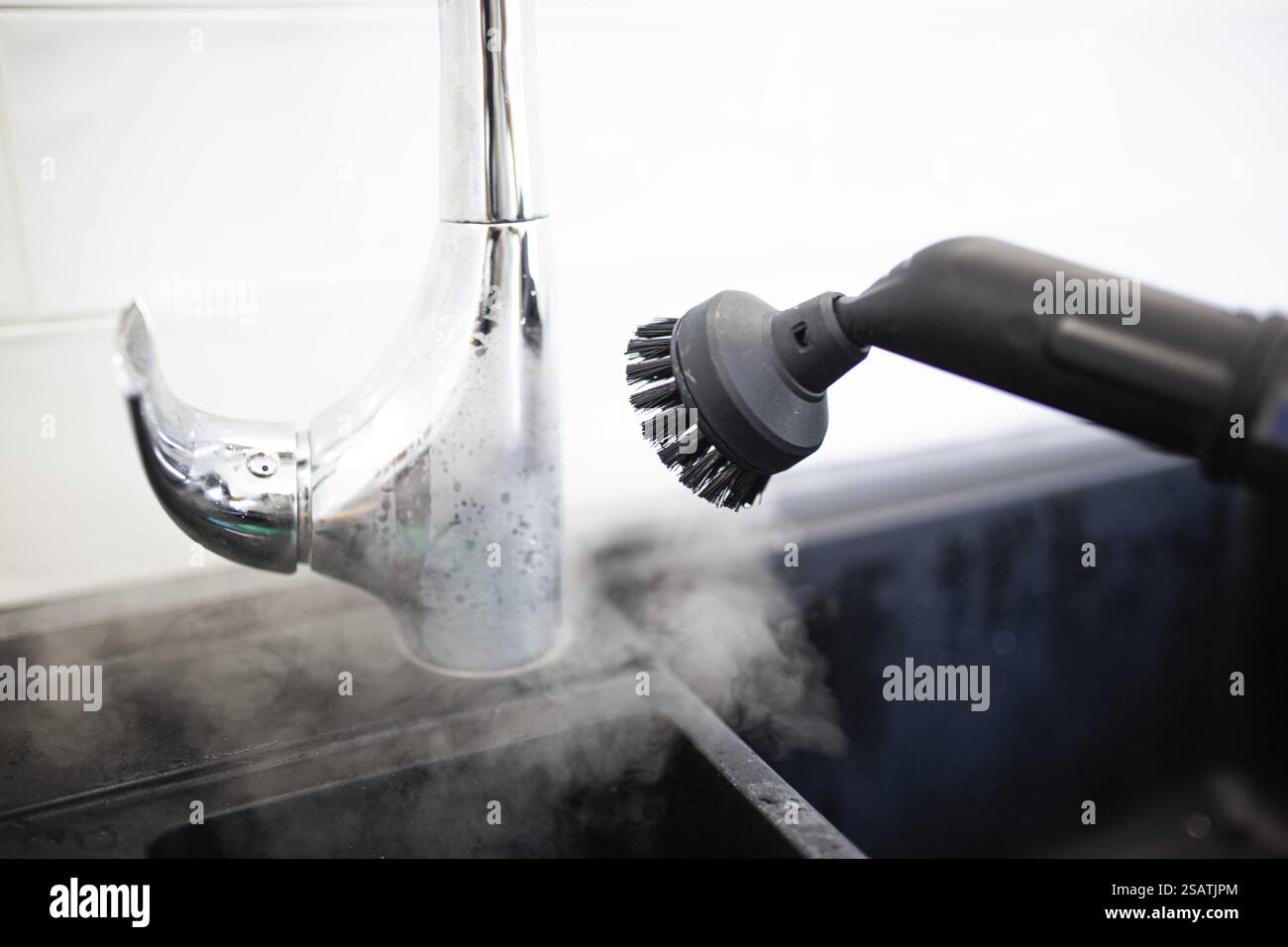 Steam cleaning a kitchen tap with a brush attachment Stock Photo - Alamy