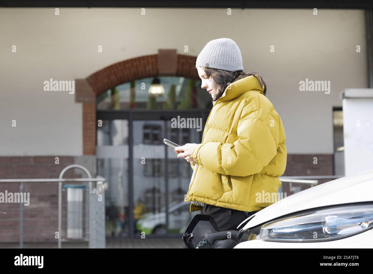 Woman with mobile phone in yellow jacket at charging station with ...