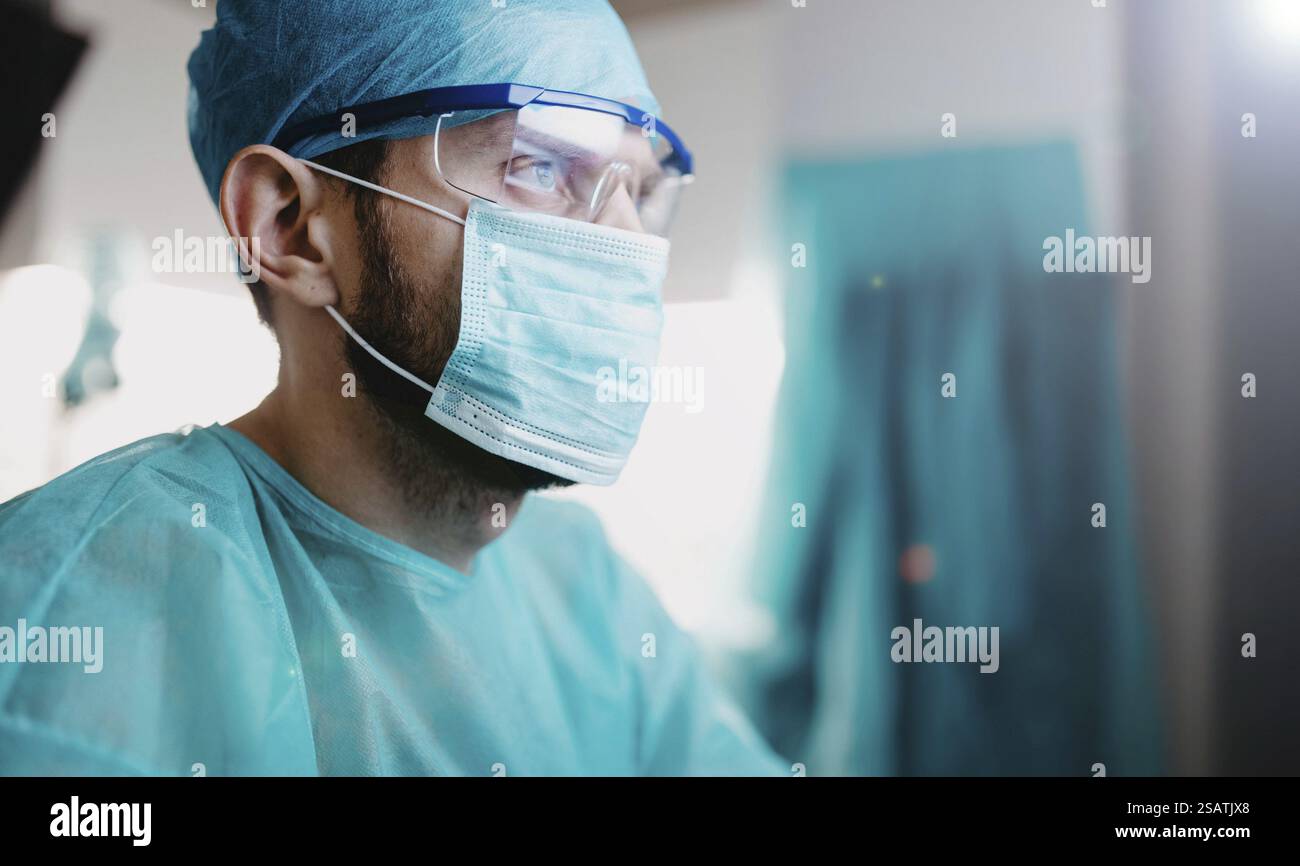 A masked surgeon in blue is looking intently ahead in an operating room ...