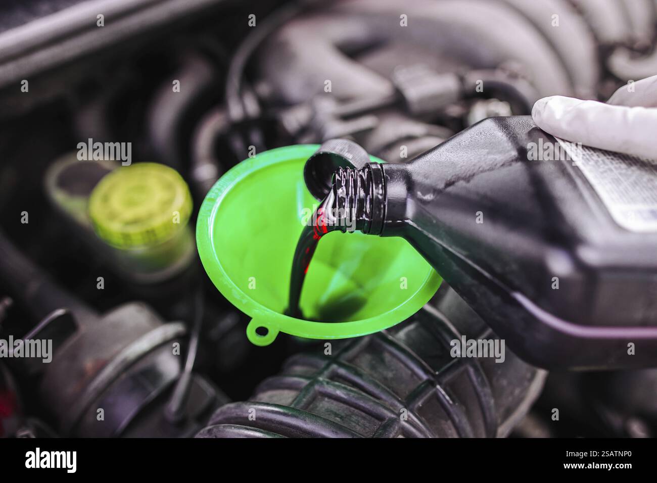 Black bottle pouring oil into a car engine with a bright green funnel ...