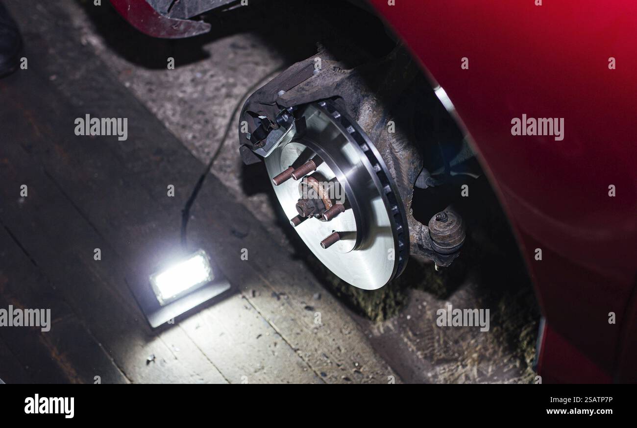 Car brake rotor under a car with a prominent red body and shadow play ...