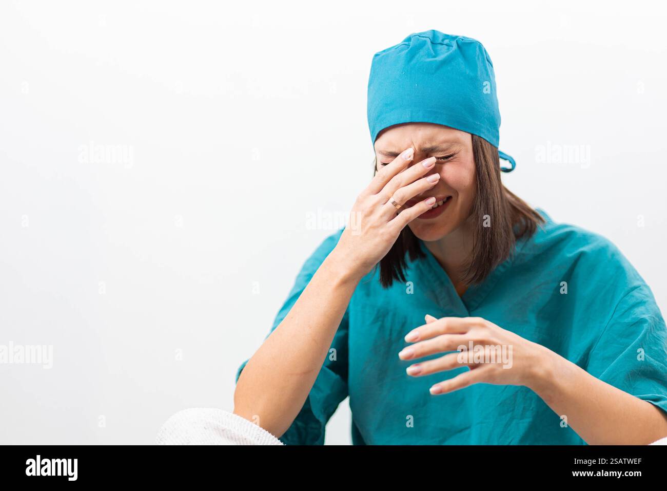 Sad nurse in teal uniform wiping tears against a white background Stock ...