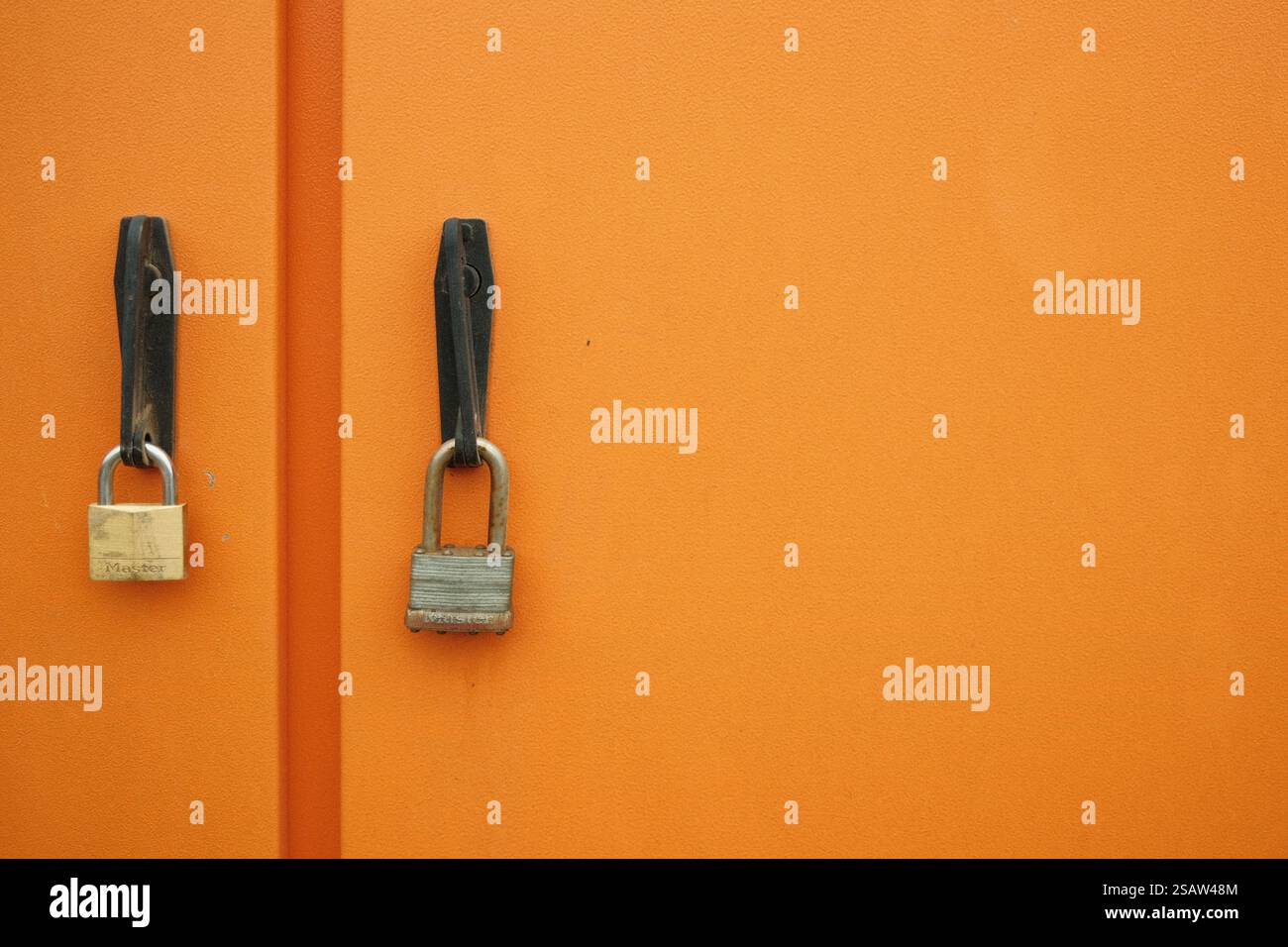 Two padlocks fastened on an orange metal door, symbolizing security ...