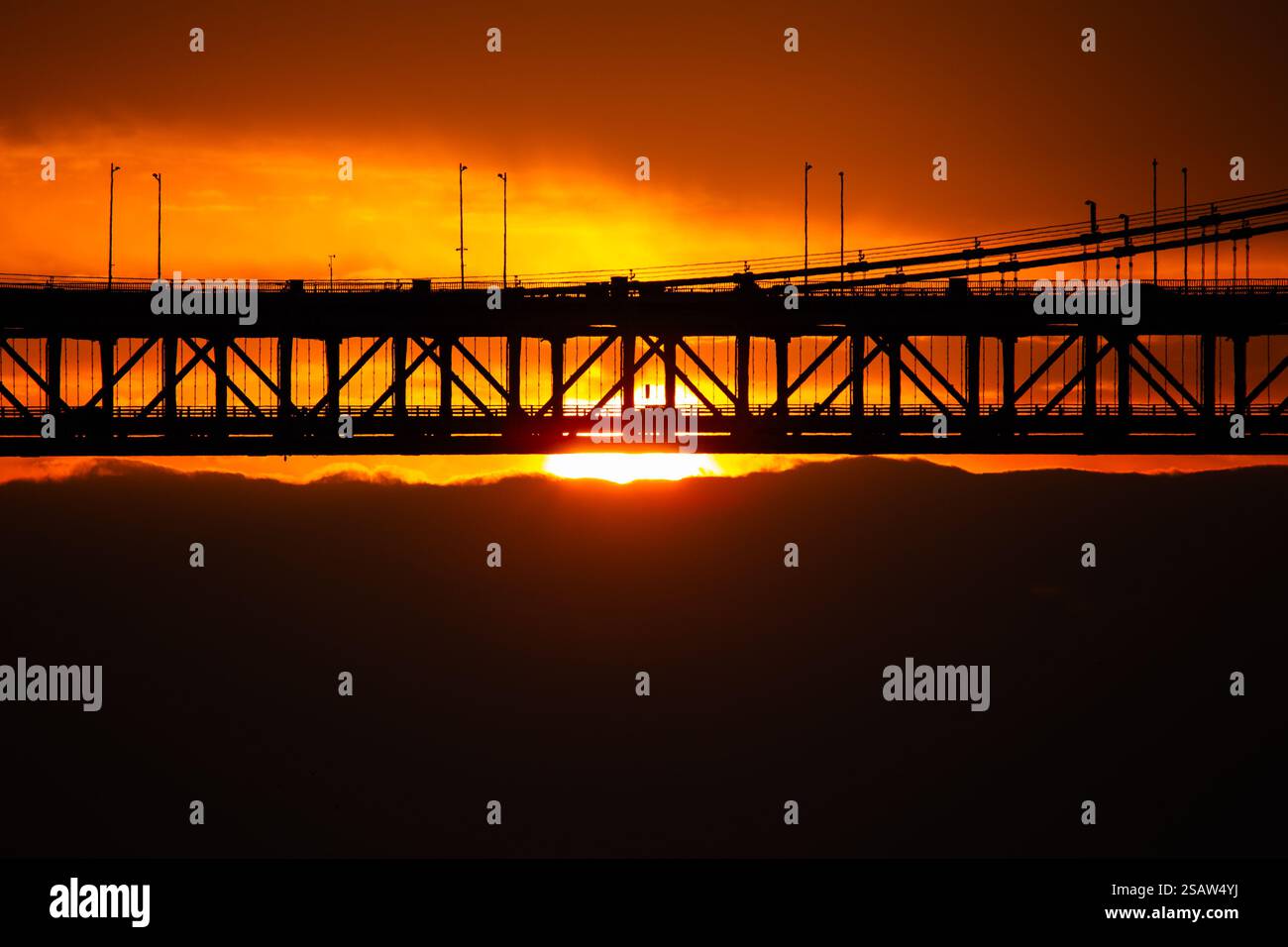 The sun rising through the clouds and cars passing through the bridge ...