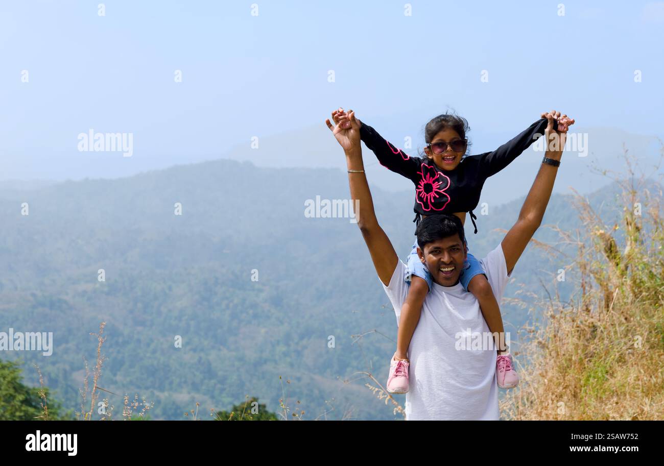 This image captures a heartwarming moment of a father carrying his daughter on his shoulders ...