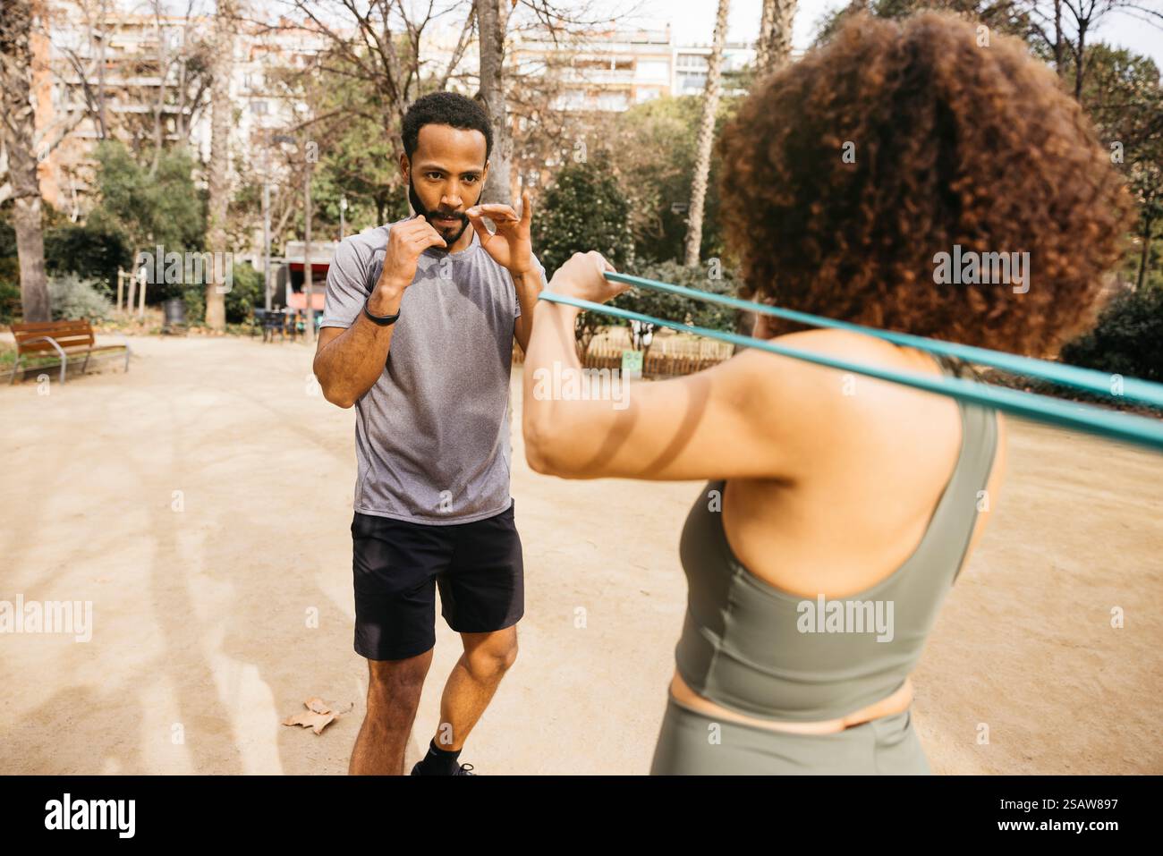 A personal trainer assists a fitness trainee with resistance band ...